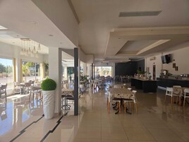 Um hall de hotel espaçoso, com diversas áreas de refeição, cozinha e uma grande janela com vista para o exterior.