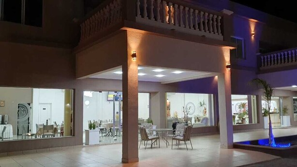 Hotel com área externa coberta, incluindo uma mesa de jantar, cadeiras, um pequeno espelho d'água e varanda com grades.