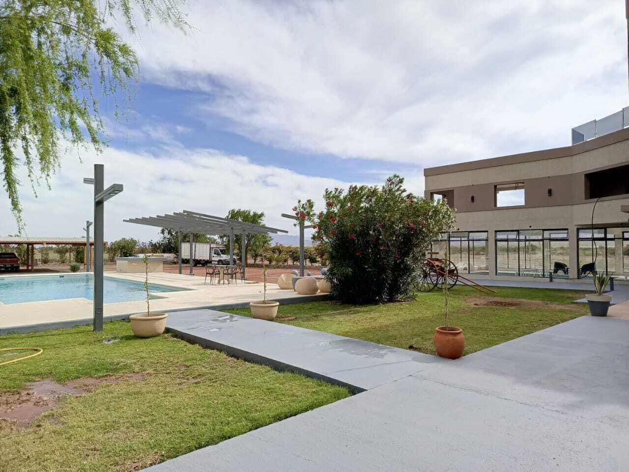 Uma área de piscina com um pérgola, mobiliário de exterior e um edifício com grandes janelas.