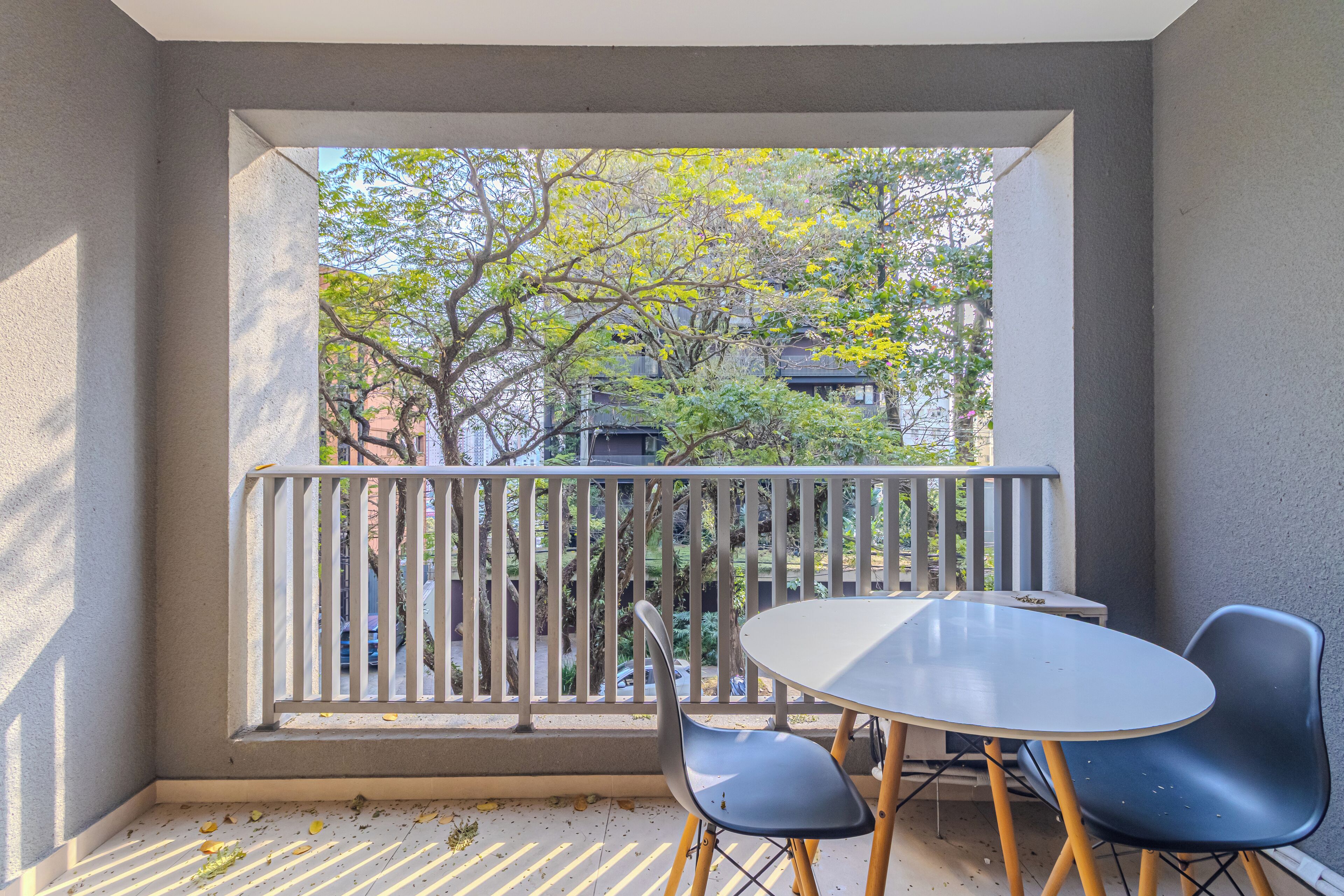 Uma varanda com mesa e cadeiras, vista para árvores e edifícios, e um corrimão.