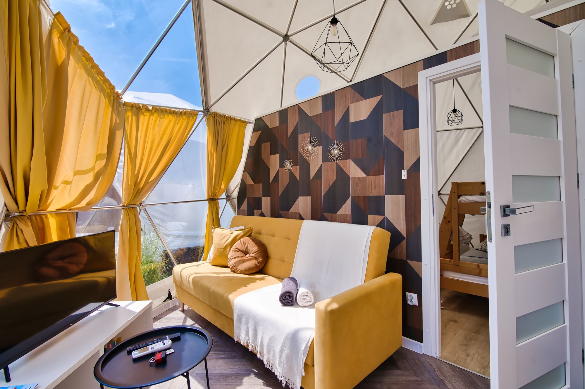 Um quarto aconchegante com um sofá amarelo, uma mesinha com um controle remoto e uma estrutura tipo tenda com cortinas amarelas.