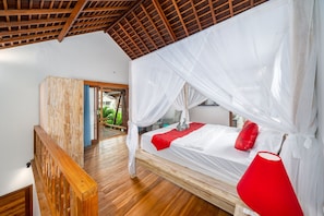 Quarto com piso de madeira, cama com dossel, abajur vermelho e vista para o exterior.