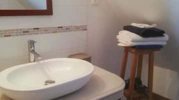 Uma casa de banho com lavatório branco, um espelho e um pequeno banco de madeira com toalhas dobradas.