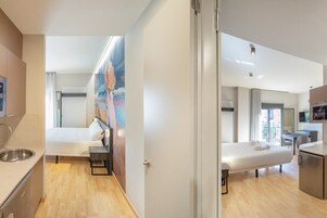 Quarto de hotel moderno com cama, escrivaninha, cozinha compacta e banheiro.