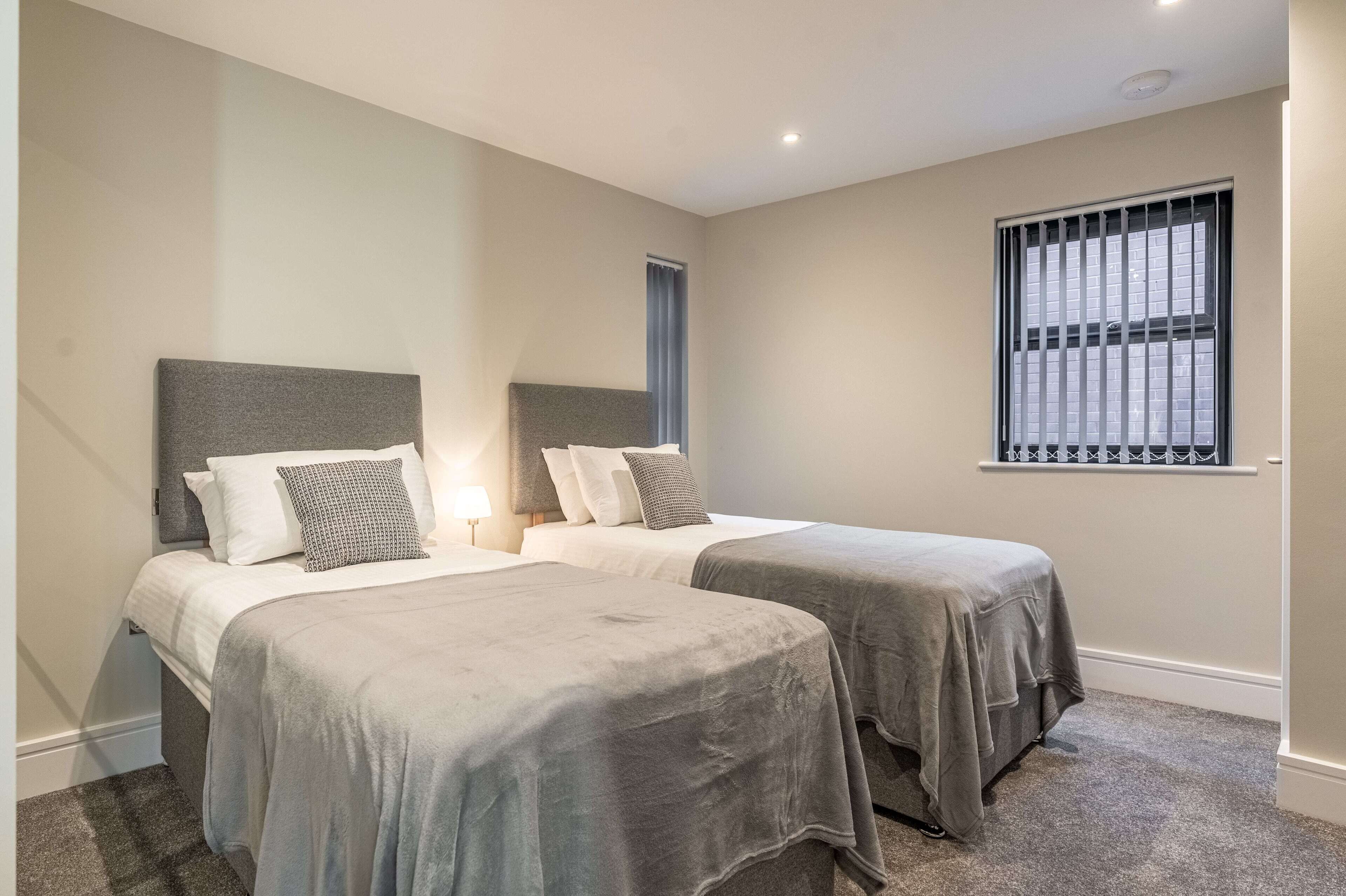 Quarto com duas camas, uma janela com grades e piso coberto por carpete.