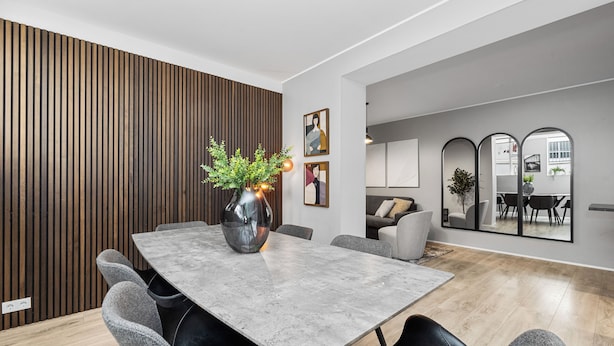 Uma área de refeições moderna com uma mesa cinza, cadeiras pretas e um vaso decorativo.