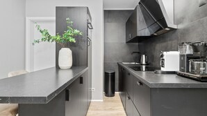 Uma cozinha moderna com armários escuros, bancada de mármore, máquina de café e lixeira.