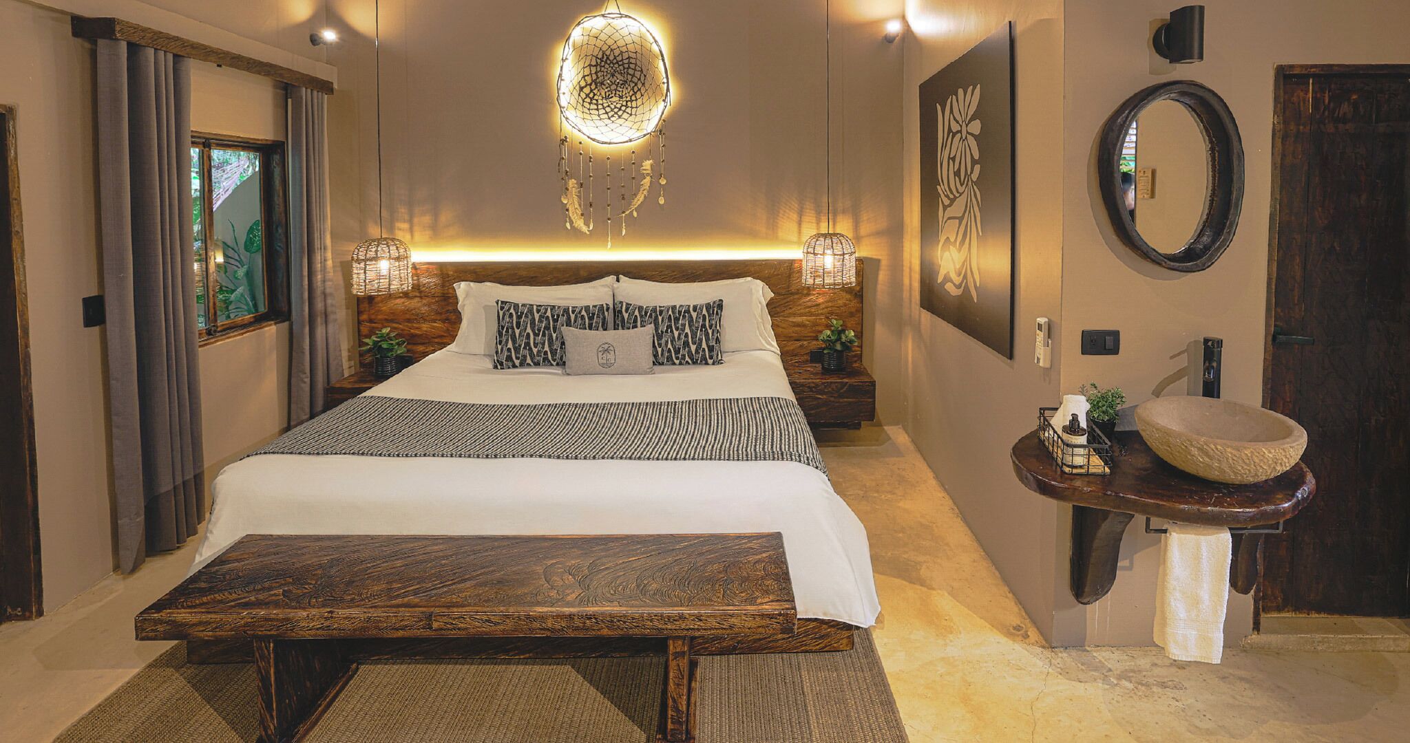 Quarto moderno com uma cama grande, mesas de cabeceira, um espelho redondo e uma pia pequena.