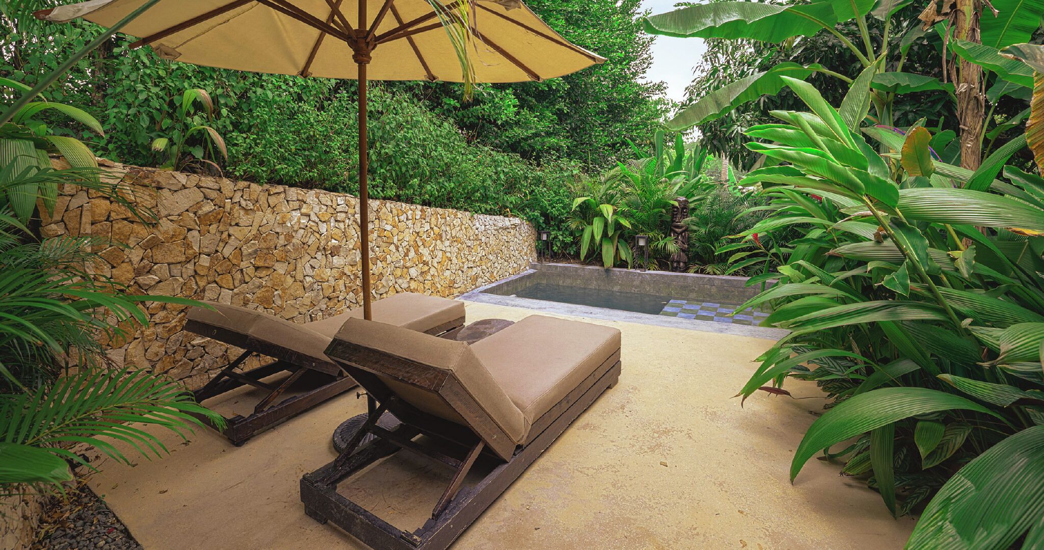 Paredes de pedra, uma pequena piscina e cadeiras de lounge sob um guarda-sol.