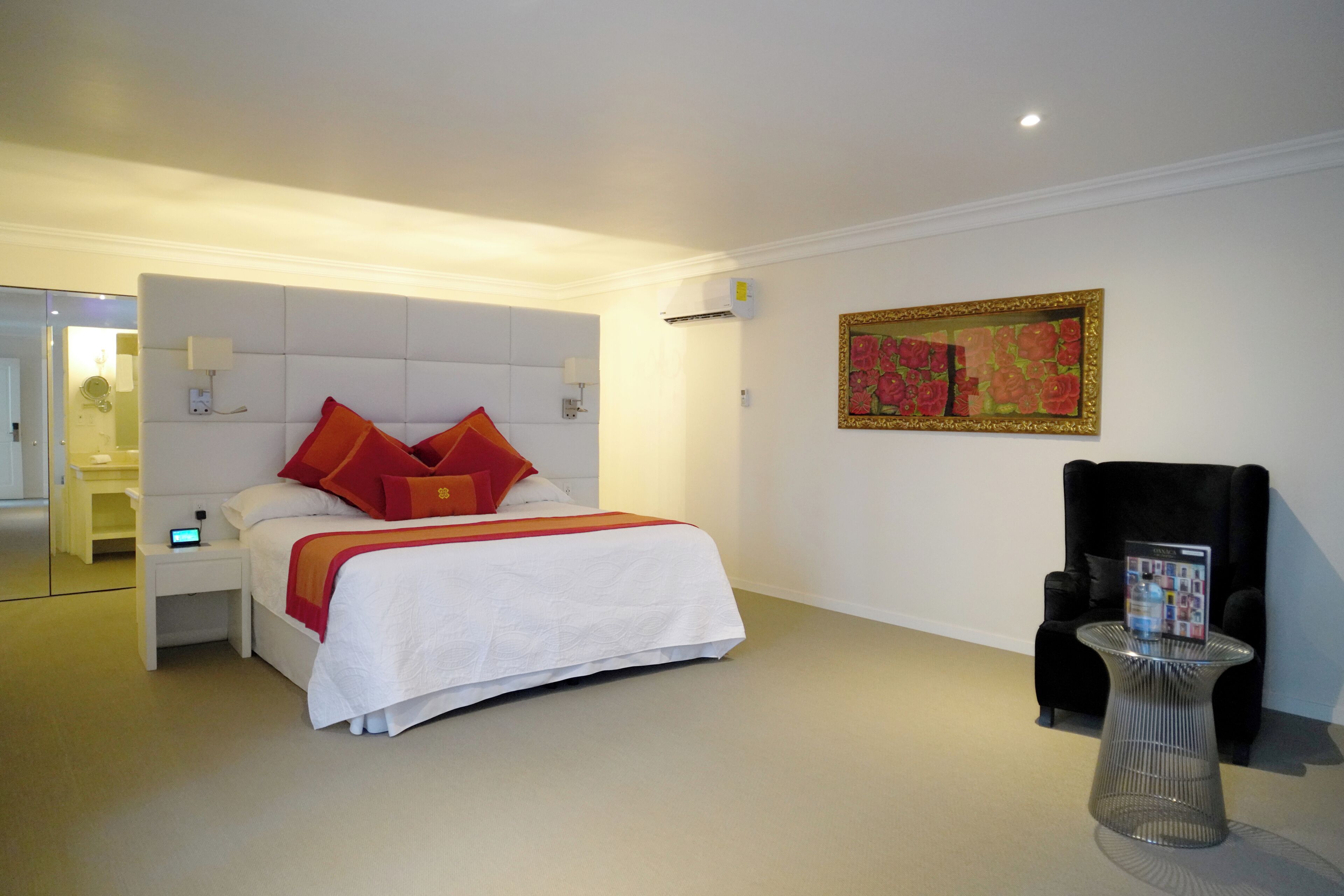 Quarto de hotel com cama, mesa de cabeceira, luminária, cadeira e uma obra de arte emoldurada na parede.