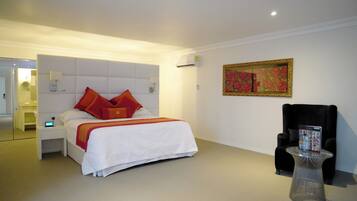 Quarto de hotel com cama, mesa de cabeceira, luminária, cadeira e uma obra de arte emoldurada na parede.
