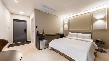 Quarto de hotel moderno com uma cama grande, uma escrivaninha, uma cadeira e uma mesinha de cabeceira com abajur.