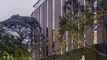 Um edifício moderno com fachada de tijolos e janelas grandes. Há uma placa com 'Le Folage Boutique Hotel' e o logotipo de 'SUMO GROUP'.