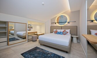 Um quarto moderno com uma cama grande, mesas de cabeceira, um espelho e uma luminária redonda na parede.