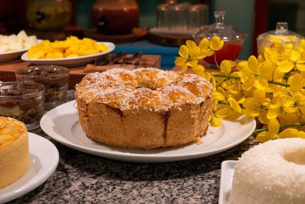Uma mesa de sobremesas com um bolo bundt, frutas e flores.