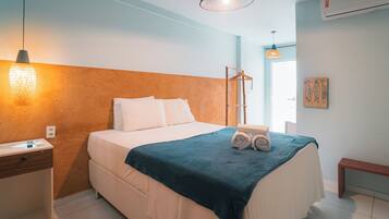Quarto com cama, mesa de cabeceira, luminária pendente e ar-condicionado fixado na parede.