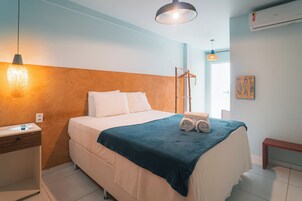 Quarto com cama, mesa de cabeceira, luminária pendente e ar-condicionado fixado na parede.