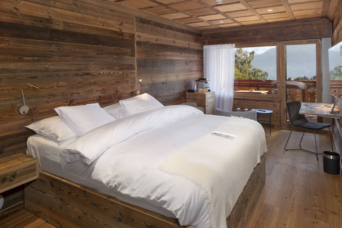 Quarto de cabana de madeira com cama, escrivaninha e vista para o exterior.