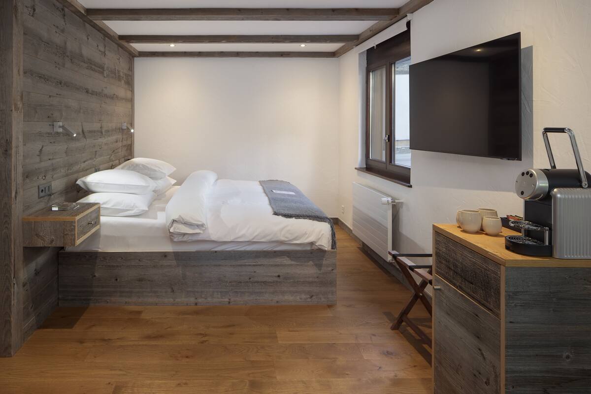 Um quarto com uma cama de madeira, uma televisão na parede e uma pequena mesa com chávenas.