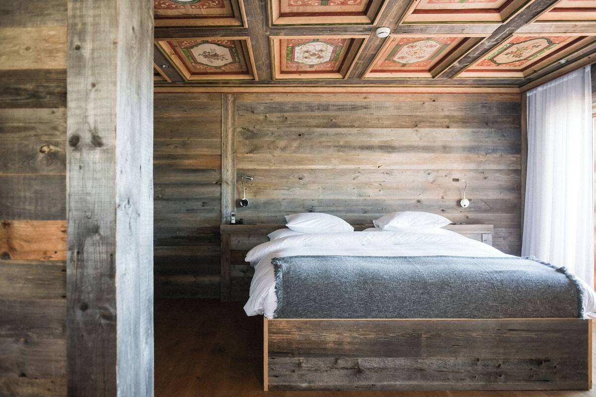 Um quarto de madeira com cama, mesa de cabeceira e teto com azulejos decorativos.