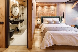 Quarto moderno com piso de madeira, uma cama grande com roupa de cama branca, cabeceira verde e parede de pedra.
