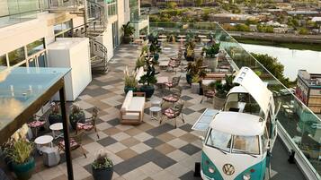 Terraço no telhado com área de estar ao ar livre, plantas em vasos e um ônibus VW antigo.