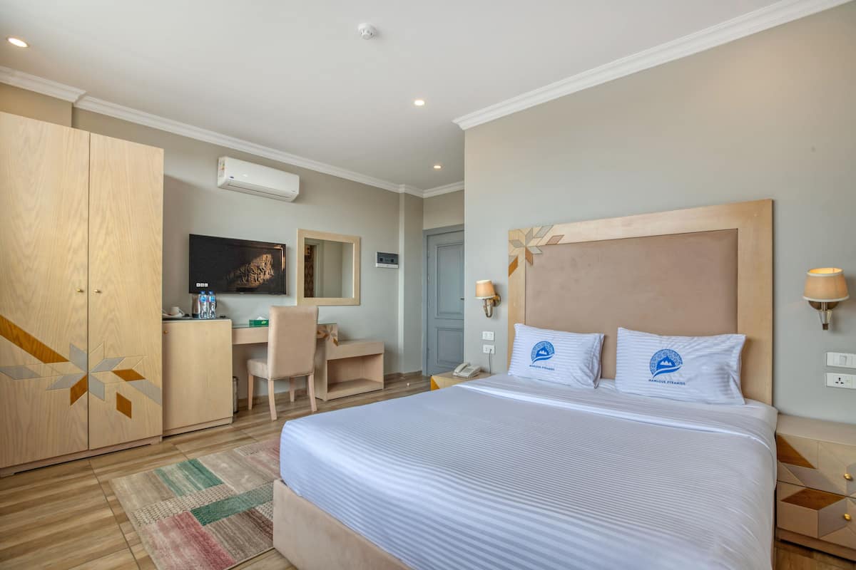 Quarto de hotel com uma cama grande, uma escrivaninha, uma cadeira, um guarda-roupa e uma televisão.