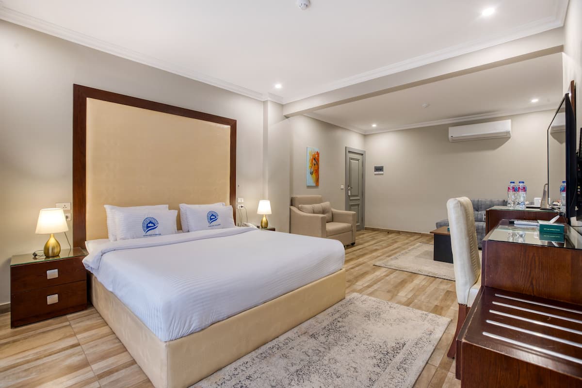 Quarto de hotel com uma cama grande, uma escrivaninha, uma cadeira, um sofá e uma televisão.