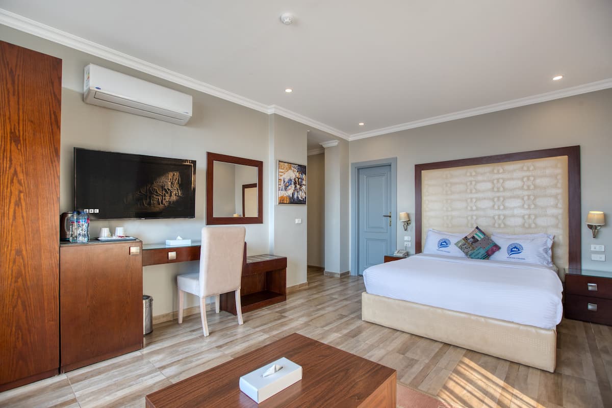 Quarto de hotel com uma cama, uma escrivaninha, uma cadeira, uma mesa de centro, um ar condicionado e uma porta.