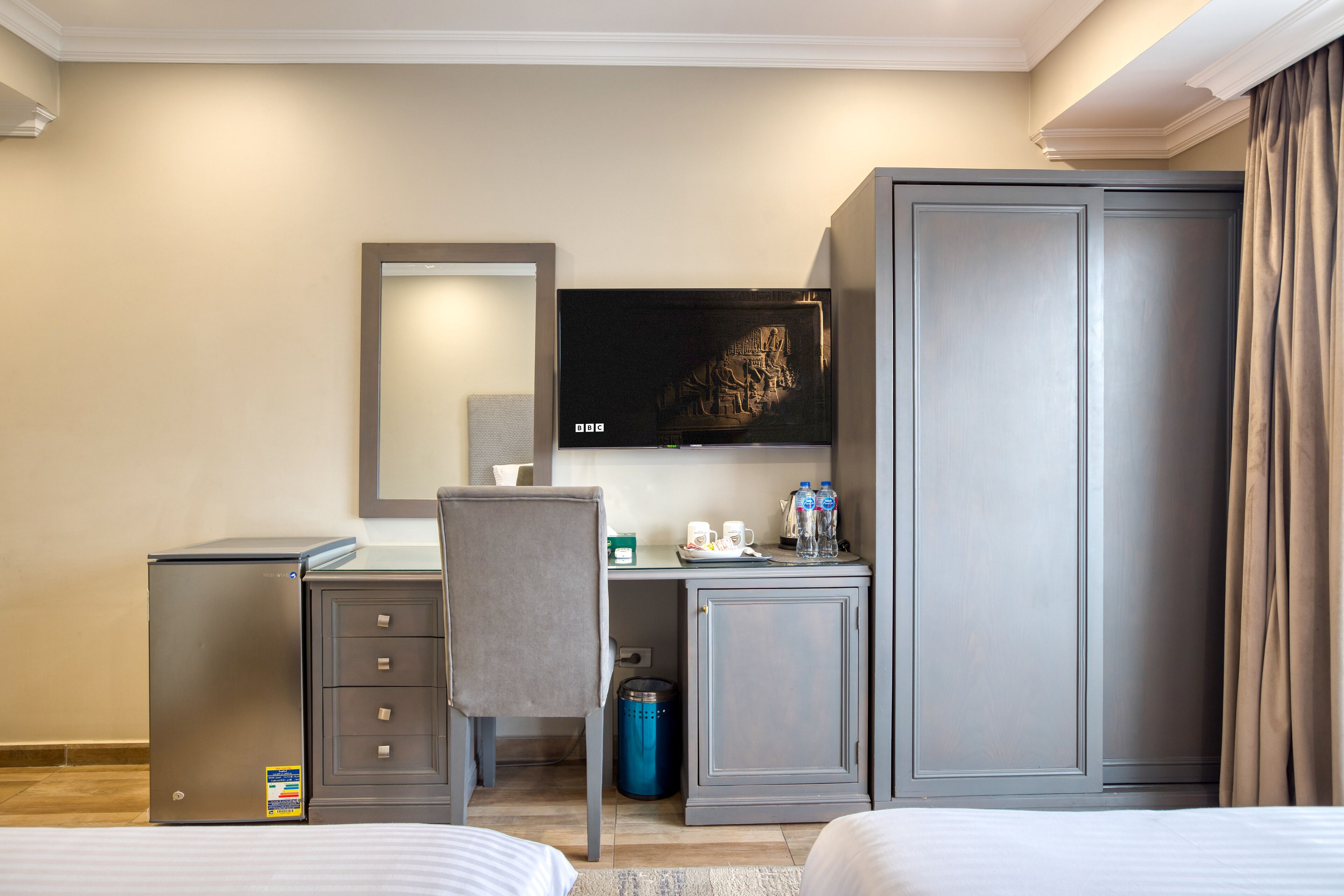 Quarto de hotel com uma cama, uma escrivaninha com cadeira, televisão, guarda-roupa e um cesto de lixo.