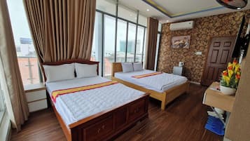Quarto de hotel com duas camas de madeira, amplas janelas, vista para a cidade e um detalhe decorativo na parede.