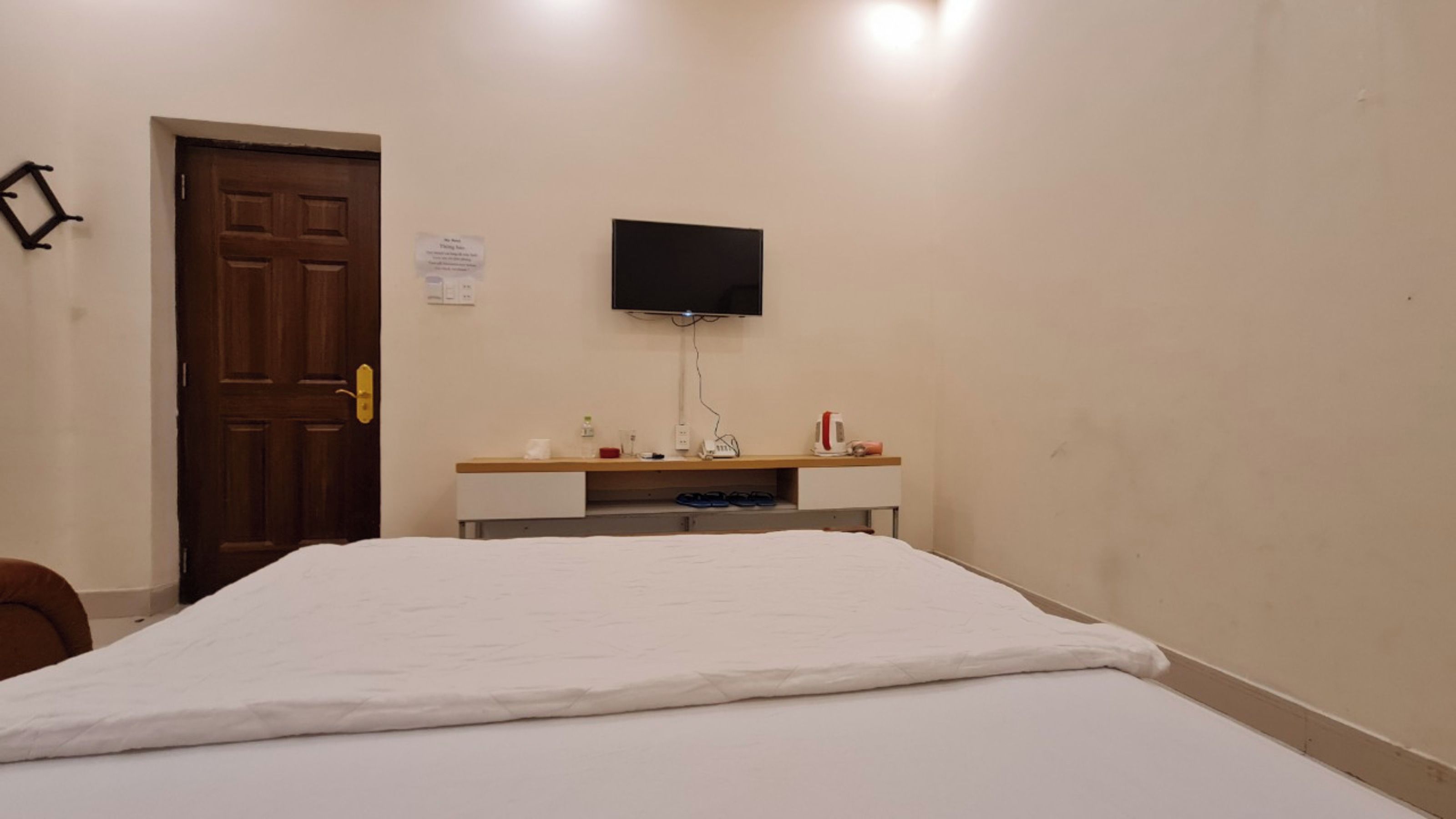 Quarto com cama, escrivaninha com televisão de tela plana, porta e placa fixada na parede.