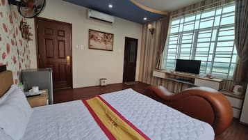 Quarto de hotel com cama, escrivaninha com computador, televisão e janela com cortinas.