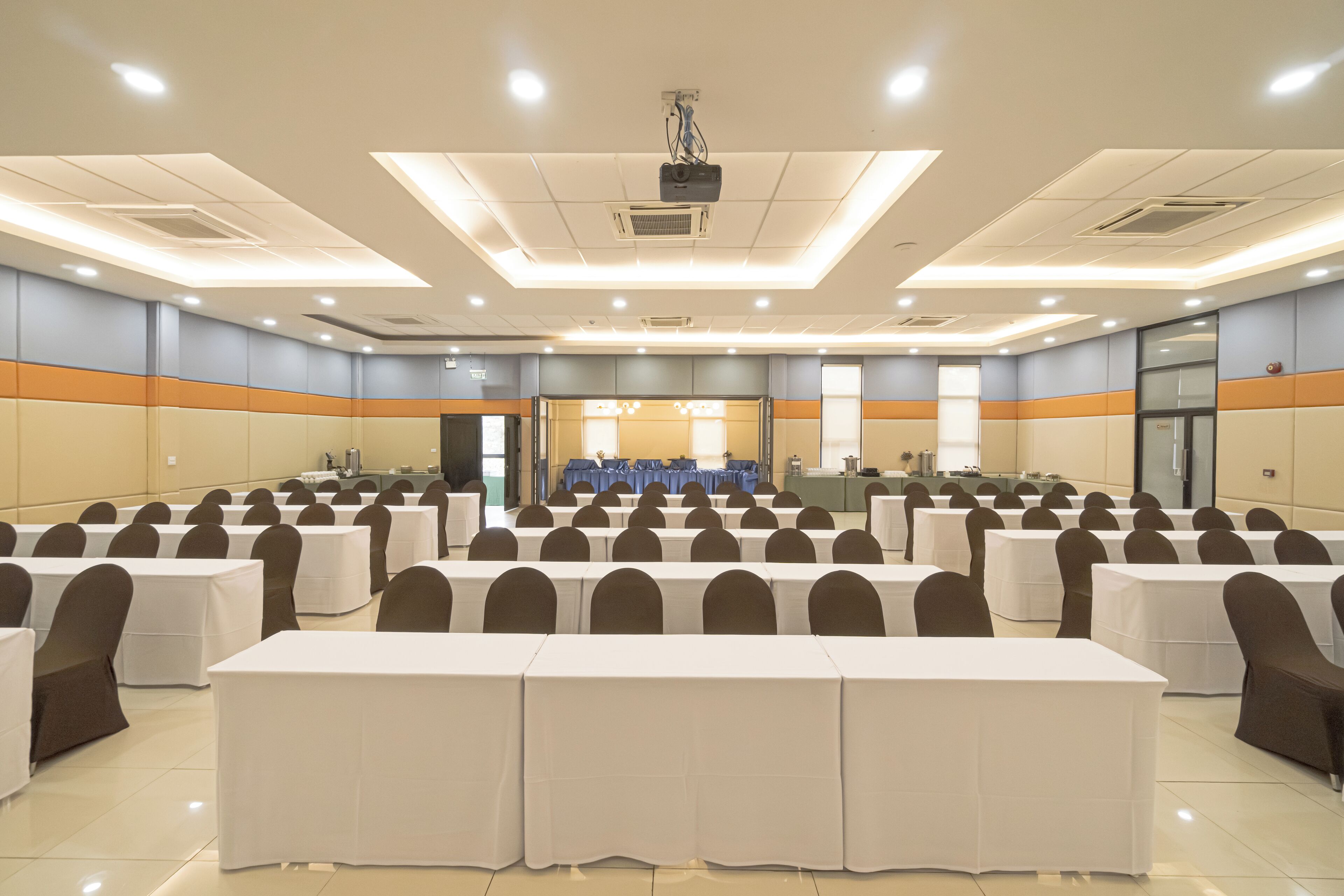Uma sala de conferências com fileiras de mesas e cadeiras, um palco e um projetor.