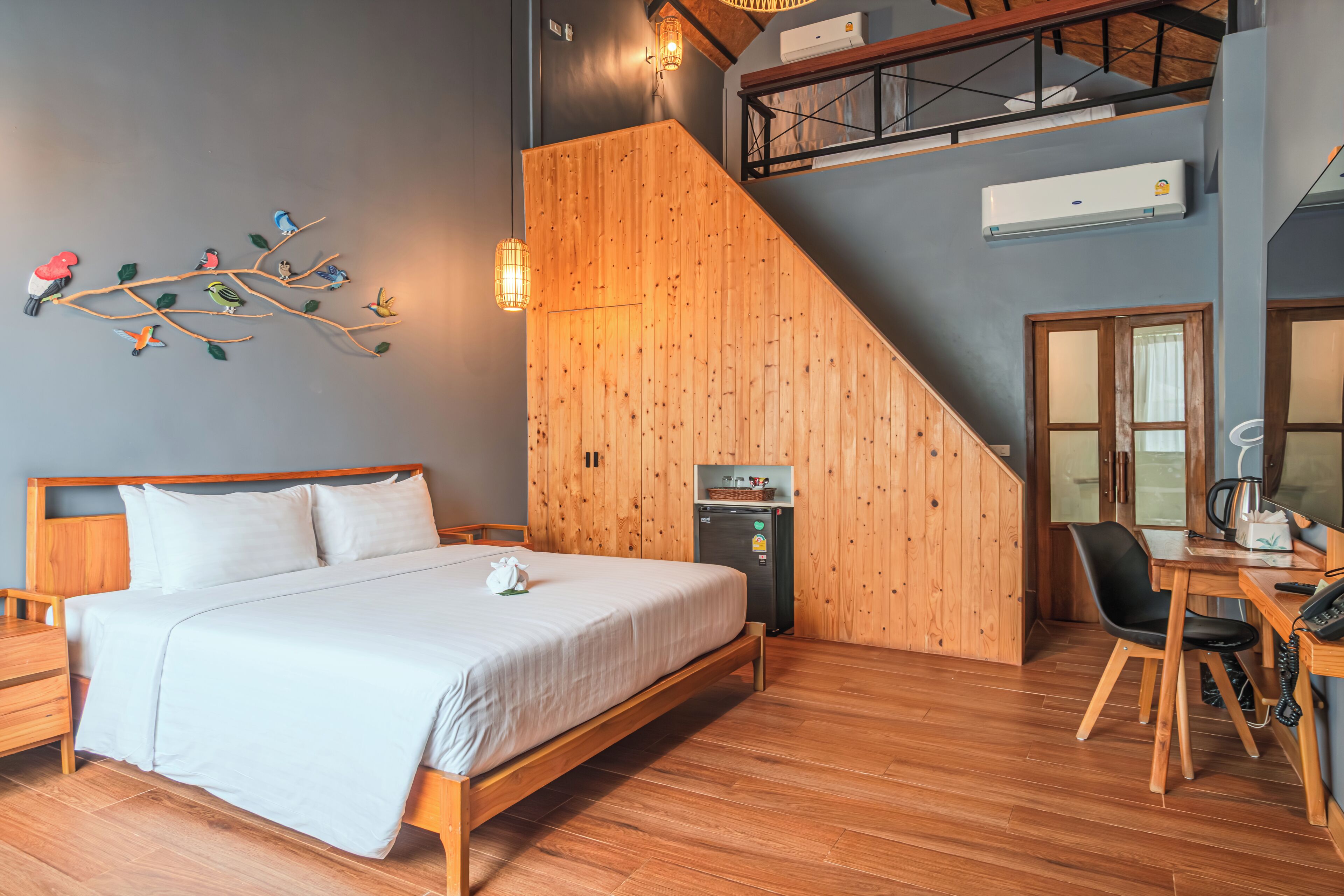 Quarto com cama de madeira, escrivaninha com cadeira, um pequeno frigorífico e escada.