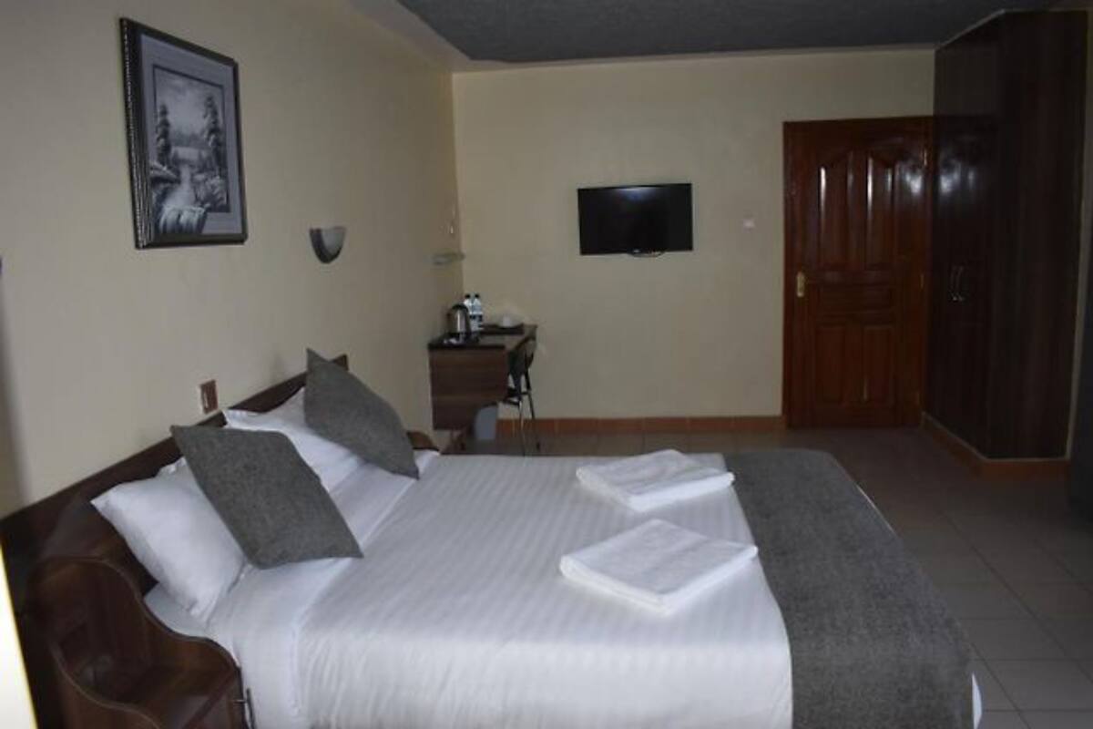 Quarto de hotel com uma cama grande, uma escrivaninha com cadeira, televisão na parede e um guarda-roupa.