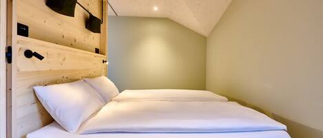 Uma cama beliche de madeira com roupa de cama branca, cabeceira com bolsos de armazenamento e teto inclinado.
