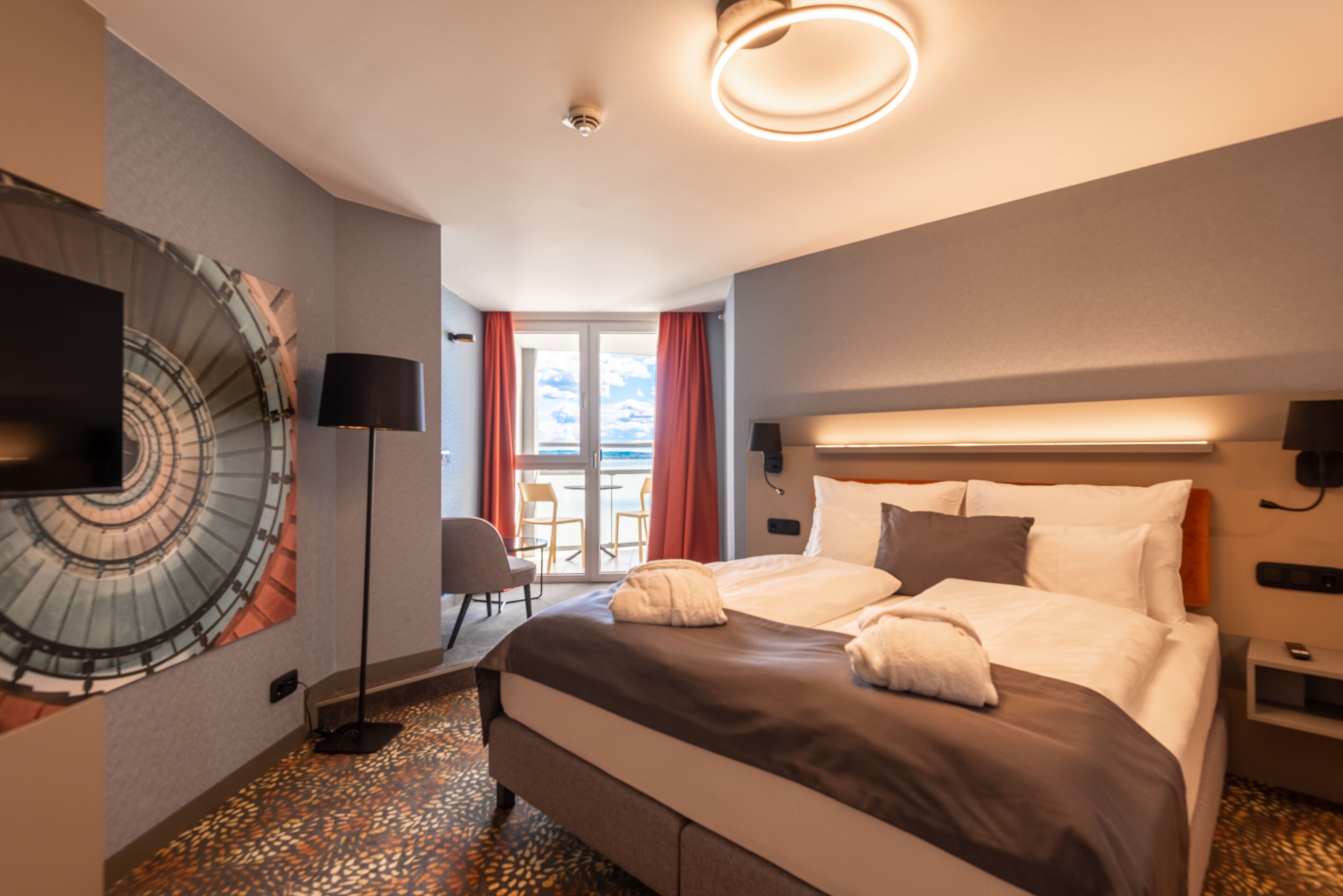 Quarto de hotel com uma cama grande, uma televisão de tela plana na parede, um abajur e vista para a varanda externa.