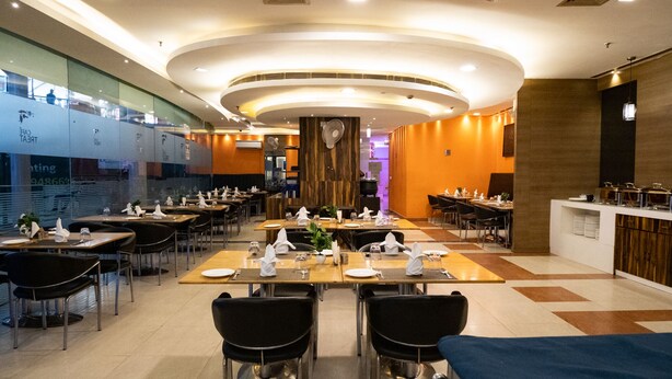 Um restaurante moderno com mesas redondas, cadeiras pretas e um pilar central de madeira.