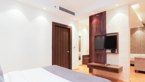 Quarto moderno com uma cama grande, uma TV fixada em um painel de madeira e um guarda-roupa de madeira.