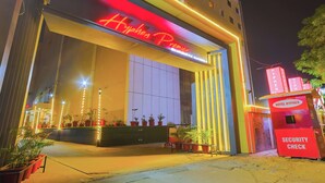 Exterior do Hotel Hyphen Premier com letreiro de neon, plantas em vasos e área de revista.