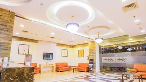 Um saguão de hotel com uma mesa de recepção, dois sofás, uma mesa de centro e um lustre.
