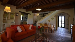 Uma sala de estar ampla com teto de madeira, um sofá vermelho, um espaço de refeições com mesa e cadeiras, e uma escada que leva a outro andar.
