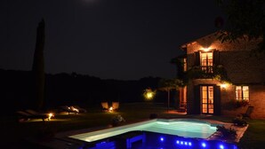 Uma casa com piscina à noite, iluminada por luzes externas.