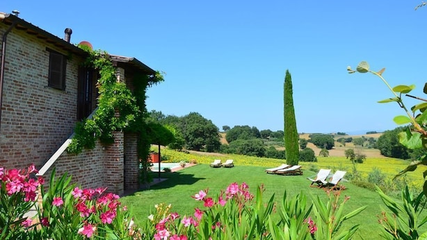 Um edifício de tijolos com um jardim, uma árvore alta e uma piscina.