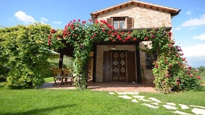 Uma casa de tijolos com varanda coberta, um banco de madeira e um jardim com flores vermelhas.