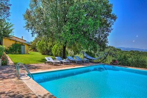 Piscina com espreguiçadeiras e rede, cercada por vegetação exuberante e céu claro.