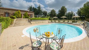 Piscina com espreguiçadeiras e mesa com bebidas, cercada por um edifício de pedra e vegeta ção.