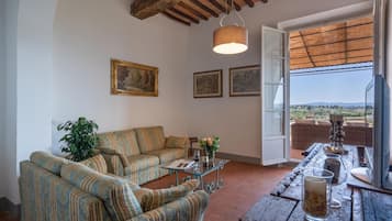 Uma sala de estar com um sofá, uma mesa de centro e vista para o campo através de uma janela grande.