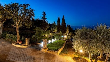 Um jardim paisagístico com caminhos, estruturas de pedra e árvores ao entardecer.